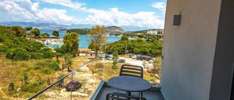 Varanda com mesa e cadeiras, vista para a praia e um estacionamento.