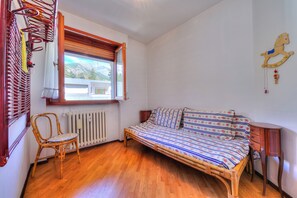 Um quarto com uma cama, uma cadeira, um radiador, uma janela e um objeto decorativo na parede.