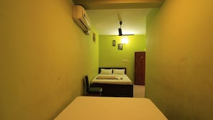 Quarto pequeno com cama, uma cadeira e um ventilador de teto.