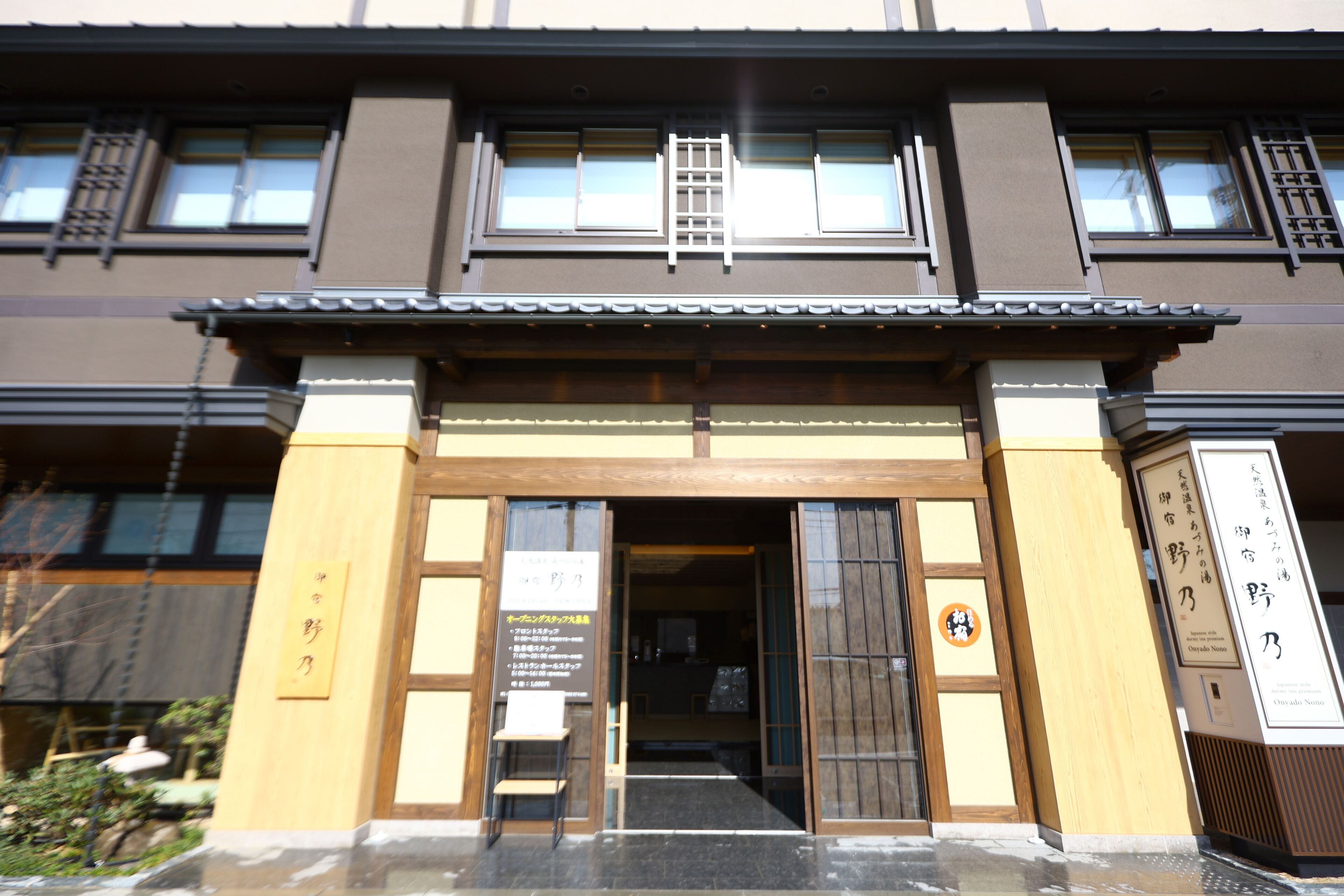 Um edifício japonês tradicional com entrada de madeira, uma placa e uma pequena área de jardim.