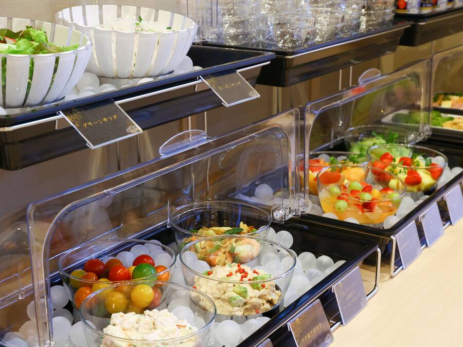Buffet com diversas opções de comida, incluindo saladas, frutas e patês.