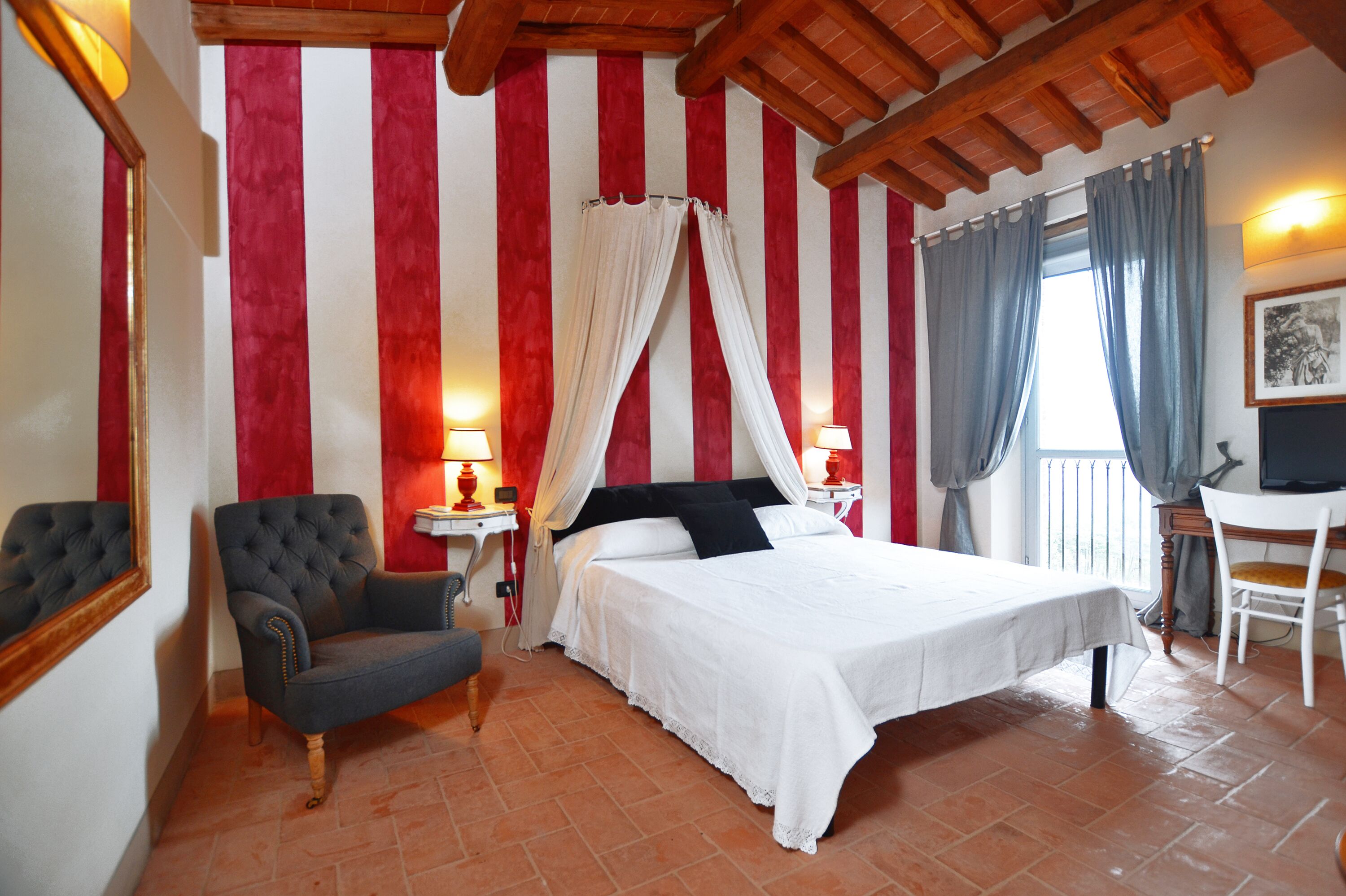 Quarto com uma cama grande, uma cadeira, uma escrivaninha e uma televisão.