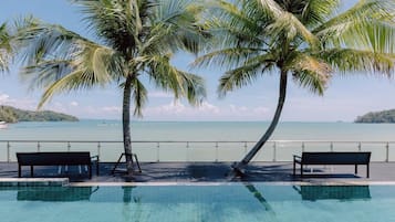 Piscina com duas espreguiçadeiras e palmeiras, com vista para o mar calmo.