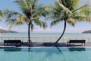 Piscina com duas espreguiçadeiras e palmeiras, com vista para o mar calmo.