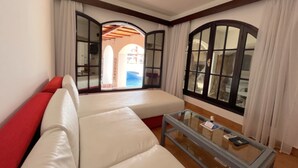Uma sala de estar moderna com um sofá, uma mesa de centro de vidro e janelas amplas com cortinas.