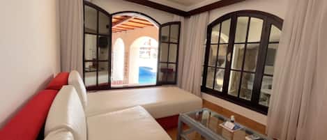 Uma sala de estar moderna com um sofá, uma mesa de centro de vidro e janelas amplas com cortinas.