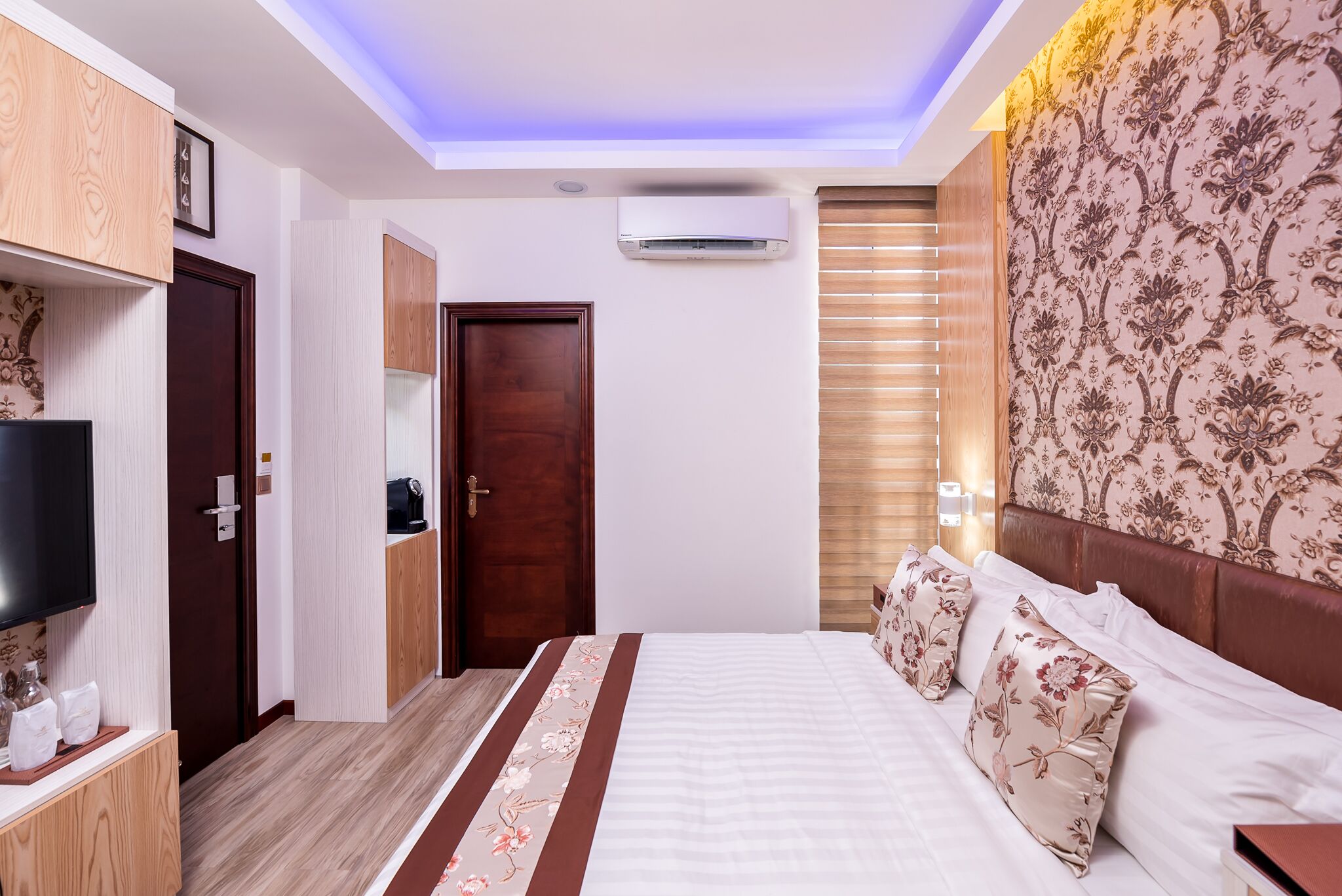 Quarto de hotel com uma cama, televisão, guarda-roupa e ar condicionado.