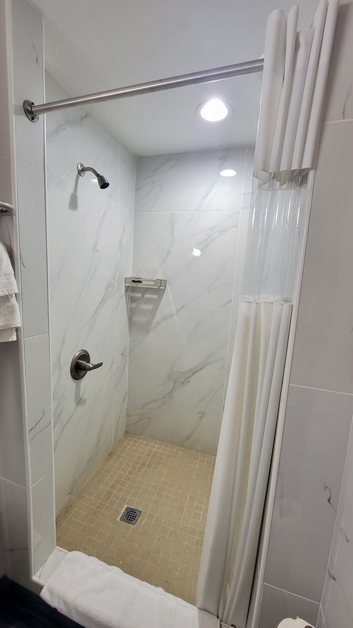 Um chuveiro sem barreiras com porta de vidro, um chuveiro manual, um porta-toalhas e um painel de controle.