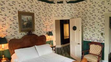 Quarto com cama, cadeira, ventoinha no teto e papel de parede floral.