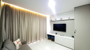 Uma sala de estar moderna com uma televisão de tela grande, um sofá e um armário com objetos decorativos.