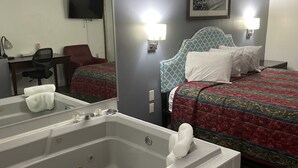 Quarto de hotel com uma banheira grande, uma secretária com cadeira, uma cama com roupa de cama estampada e uma televisão fixada na parede.