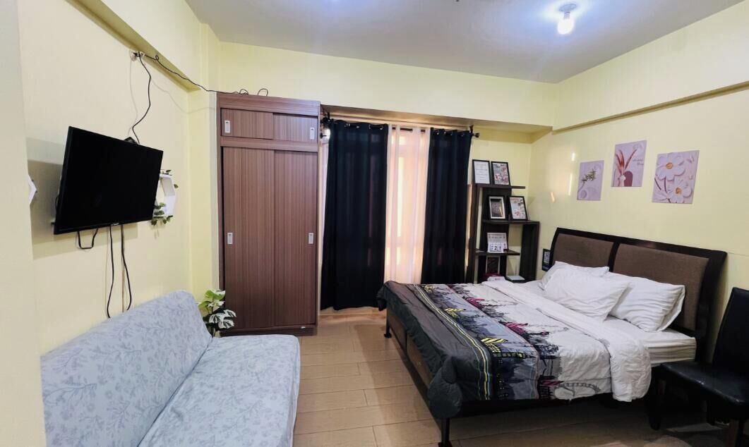 Quarto com cama, sofá, televisão, guarda-roupa e secretária.
