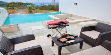 Uma área ao lado da piscina com móveis de vime, churrasqueira e uma mesa com comida e bebidas.