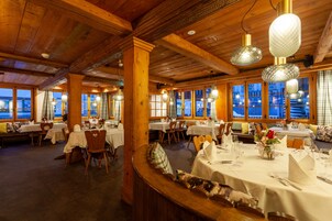 Restaurante com interiores em madeira, várias mesas preparadas para refeições e grandes janelas com vista.