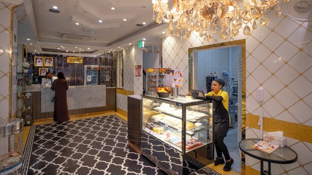 Uma área de recepção de hotel com balcão, lustre e uma vitrine com alimentos.