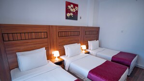 Quarto de hotel com três camas de solteiro, cabeceiras de madeira, roupa de cama branca e uma obra de arte floral vermelha na parede.