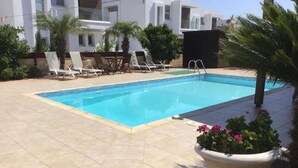 Piscina retangular com deck revestido, rodeada por espreguiçadeiras e plantas em vasos.