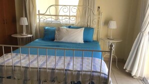 Uma cama com estrutura metálica, duas mesas de cabeceira e uma janela com cortinas.