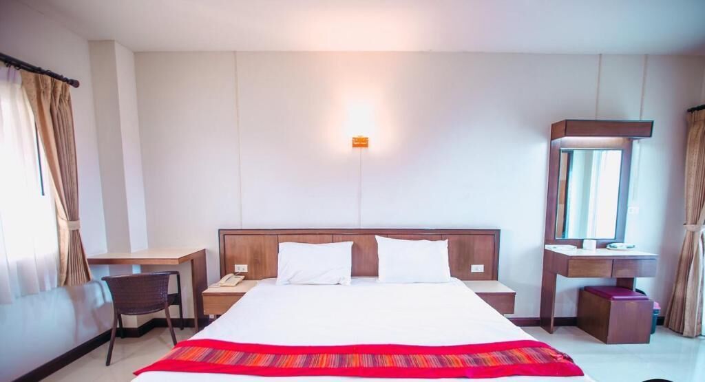 Quarto de hotel com uma cama grande, uma escrivaninha, uma cadeira, uma mesa de cabeceira, um espelho e uma janela com cortinas.
