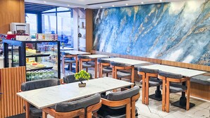 Interior de restaurante moderno com mesas e cadeiras de madeira, um balcão com itens alimentícios e um grande mural abstrato na parede.