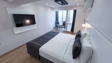 Quarto de hotel moderno com uma cama grande, uma televisão de tela plana na parede e vista para o mar pela janela.