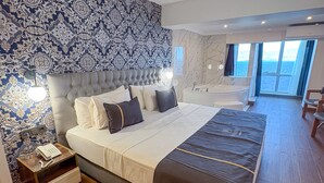 Uma cama grande com cabeceira acolchoada, mesa de cabeceira com telefone e parede estampada.