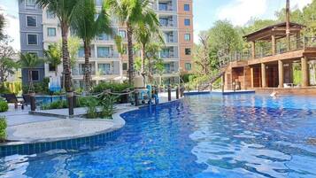 Piscina cercada por palmeiras e um edifício com várias andares e varandas.