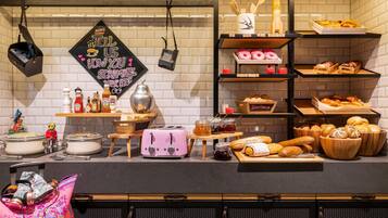 Um buffet de café da manhã com diversos alimentos, uma lousa com uma mensagem e utensílios de cozinha.