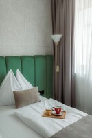 Cama bem arrumada com cabeceira verde, abajur e bandeja com xícara e pastel.
