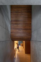Um interior moderno com teto de ripas de madeira, paredes de concreto e piso de madeira.