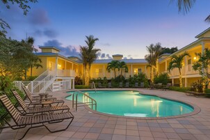 Uma área de piscina com espreguiçadeiras, escadas e um edifício com varandas.