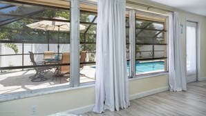 Uma sala de sol com grandes janelas, piscina e mobiliário de exterior.
