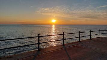 Um pôr do sol sobre o oceano, com um calçadão de concreto e grades de metal.