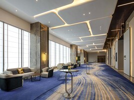 Um saguão de hotel moderno, com carpete azul, áreas de estar e janelas amplas.