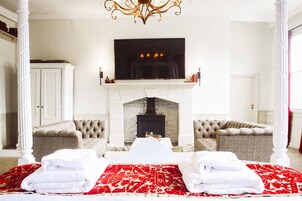 Quarto com lareira, duas poltronas, cama com colcha estampada em vermelho e branco, e televisão sobre a lareira.