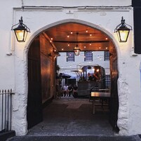Uma entrada em arco com luminárias pendentes, uma escadaria e uma área de estar ao ar livre.