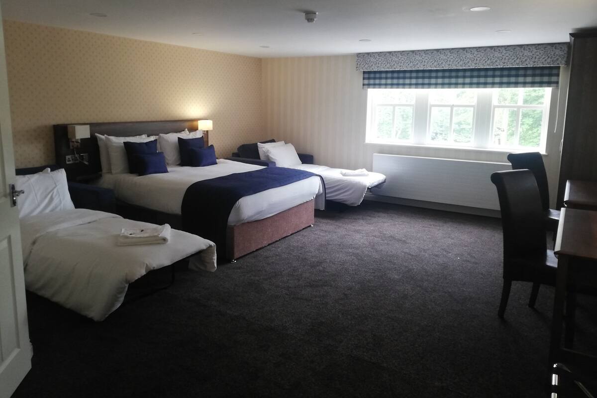 Quarto de hotel com duas camas, uma escrivaninha e janela com vista.