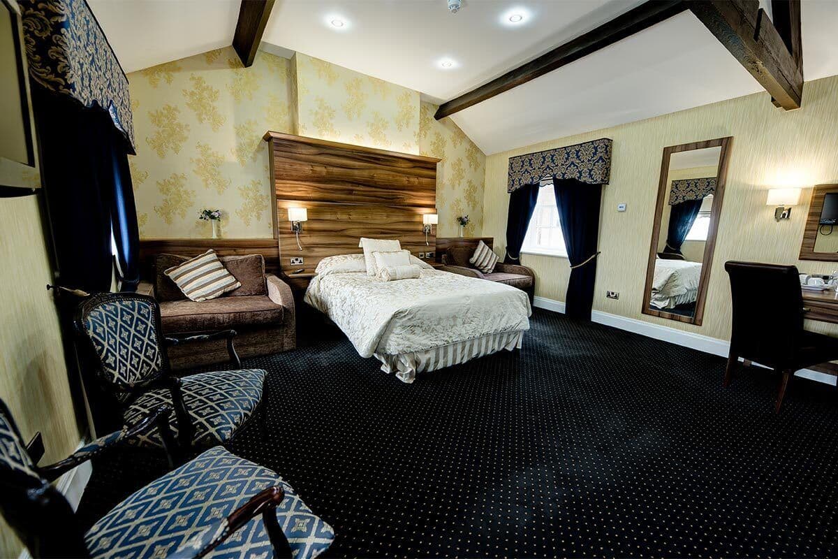 Quarto de hotel com uma cama grande, cabeceira de madeira, duas mesas de cabeceira, um espelho e um tapete estampado.