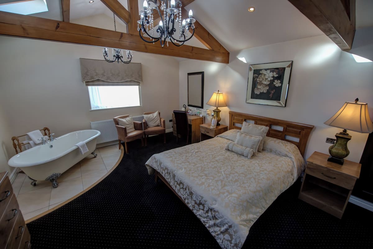Quarto com uma cama grande, toucador com banheira, lustre e janela com vista.