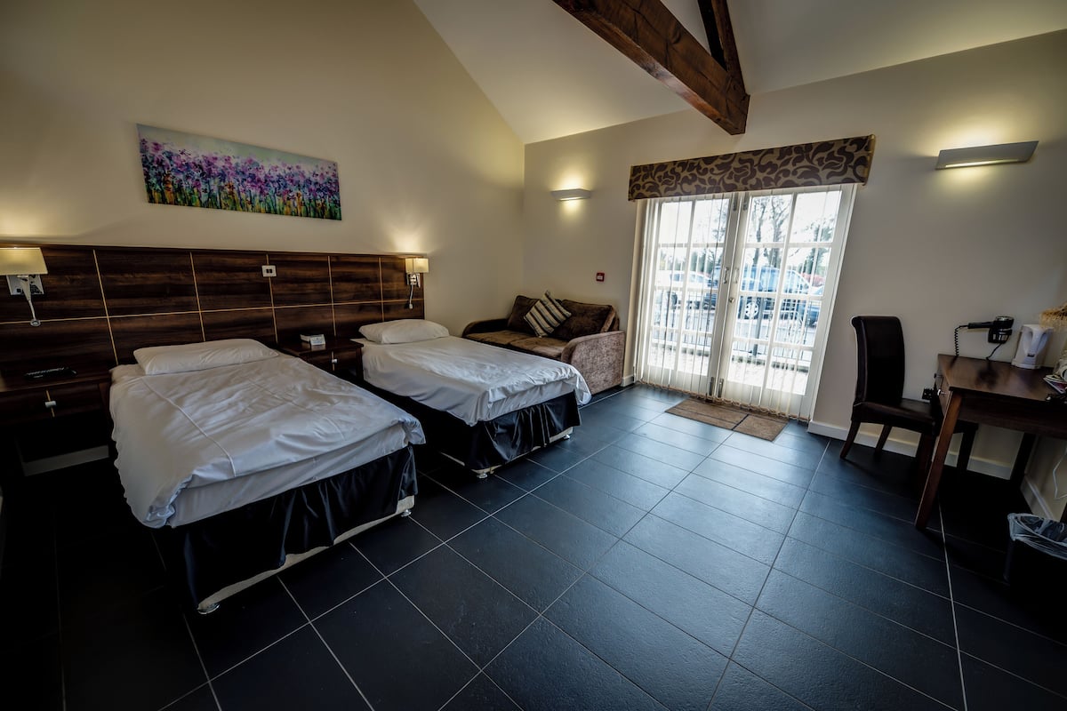 Quarto de hotel com duas camas, um sofá, uma escrivaninha e uma janela grande.