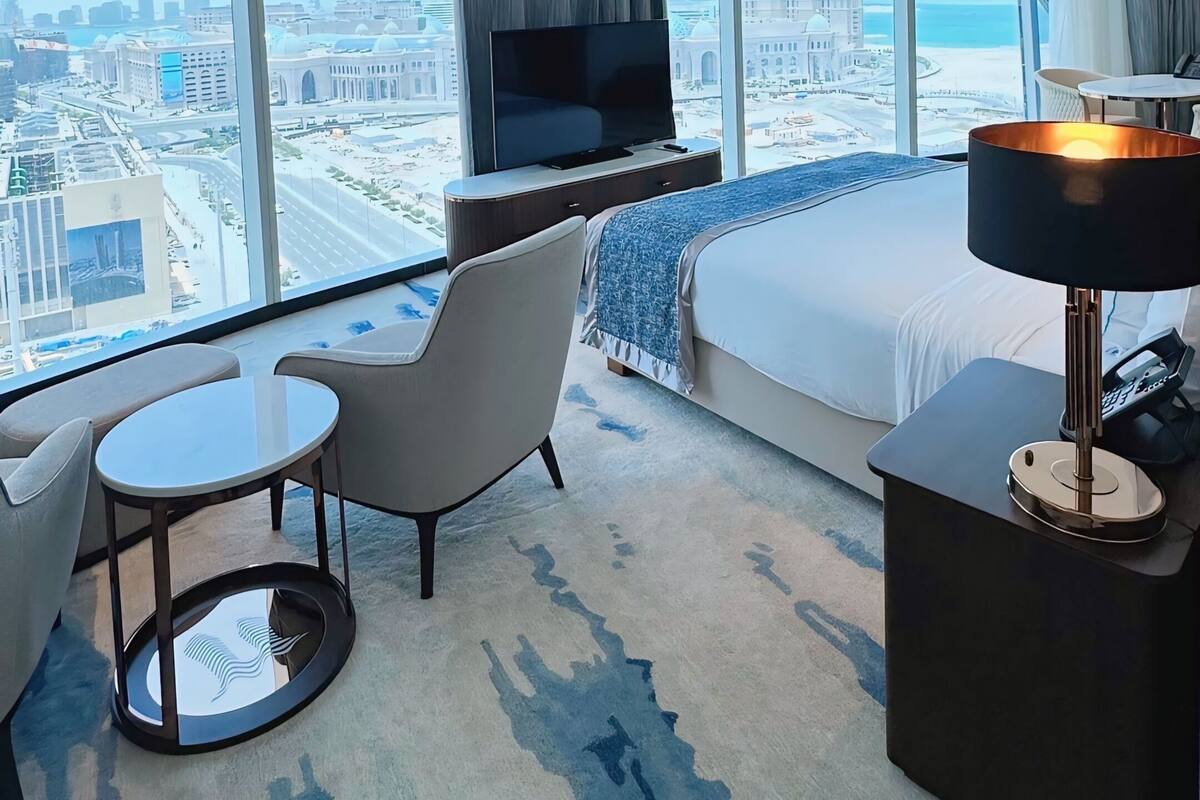 Quarto de hotel moderno com uma grande janela, cama, televisão, escrivaninha e cadeira.