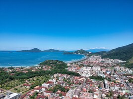 Paisagem costeira com uma mistura de edifícios residenciais e comerciais, céu azul límpido e vista para o oceano e montanhas ao longe.