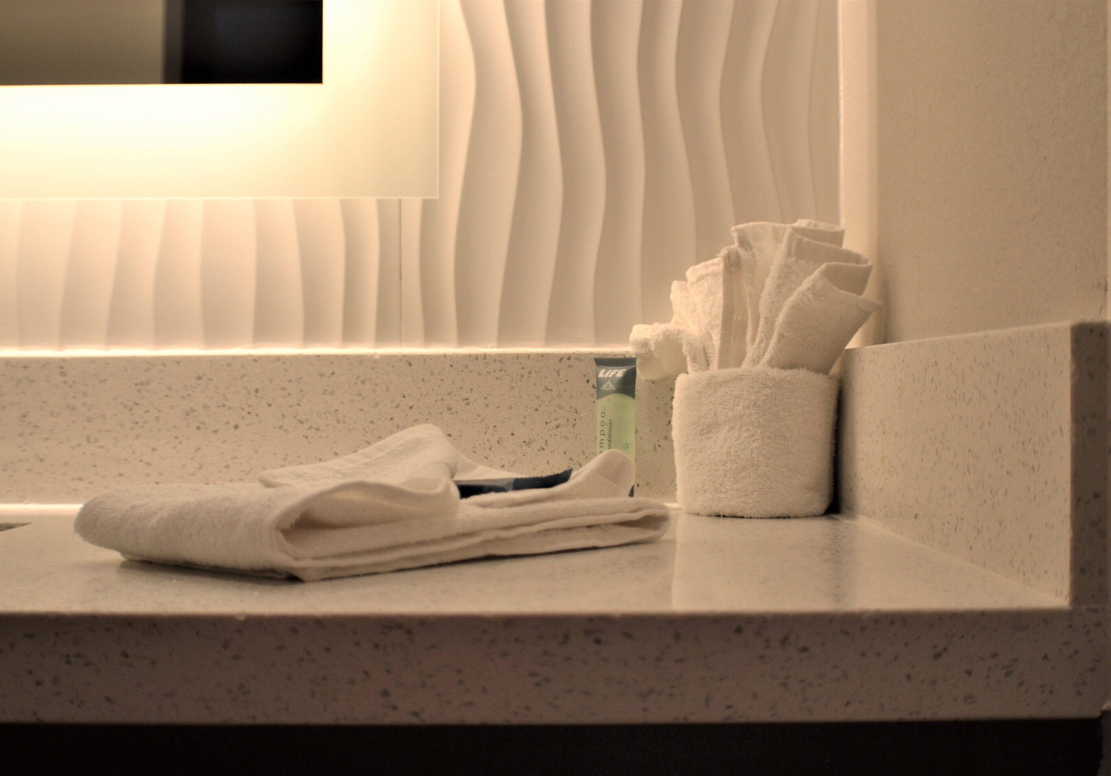 Uma bancada de banheiro com uma toalha dobrada, uma garrafa de shampoo e um porta-toalhas.