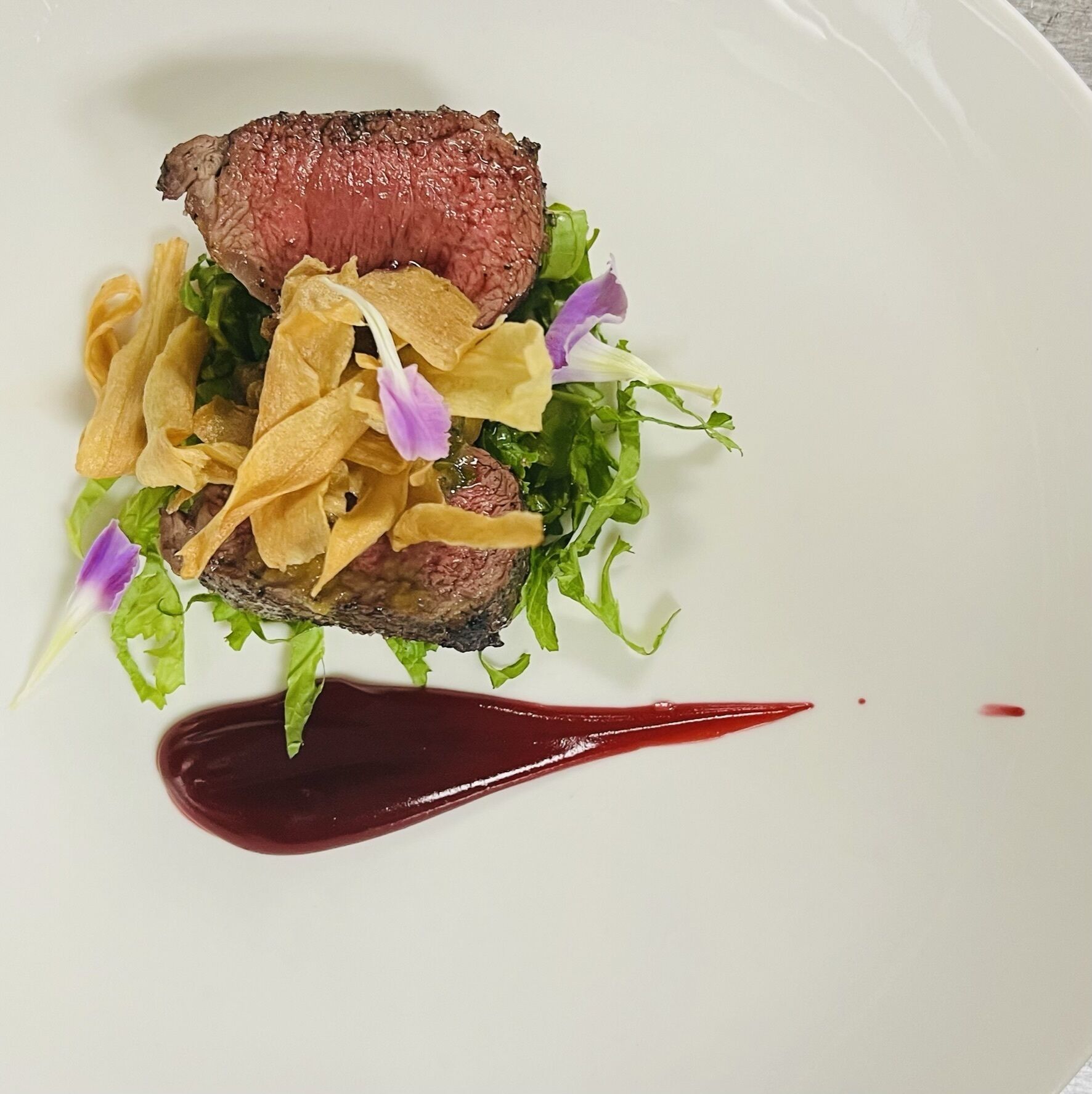 Um prato com bife, vegetais verdes e molho vermelho.