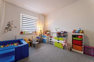 Um quarto infantil com piscina de bolinhas, prateleiras cheias de brinquedos e uma janela com persianas.