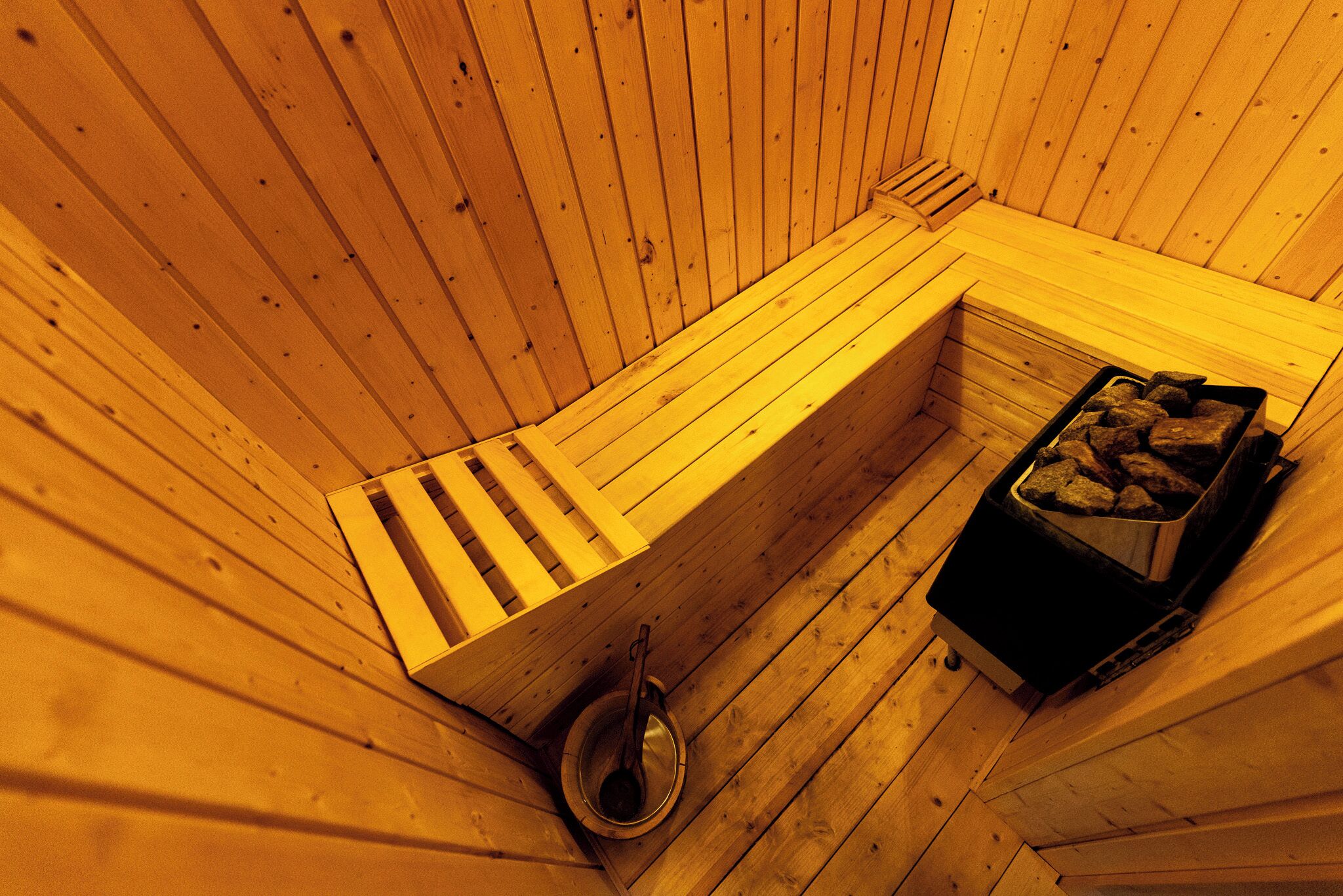 Uma sauna com paredes e bancos de madeira, uma bacia de metal e um recipiente com pedras.