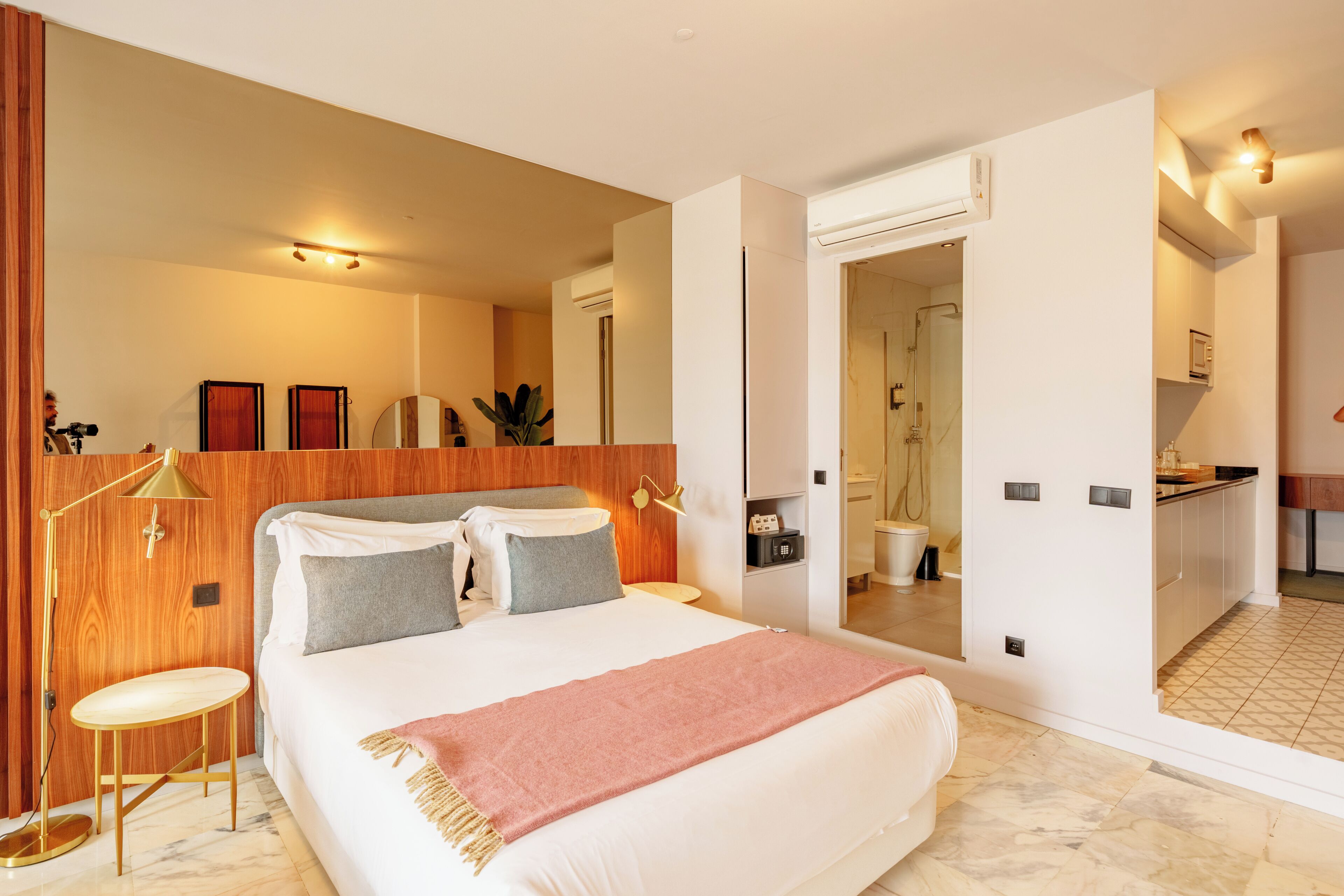 Quarto moderno com uma cama grande, mesas de cabeceira, uma luminária de chão e vista para o banheiro.