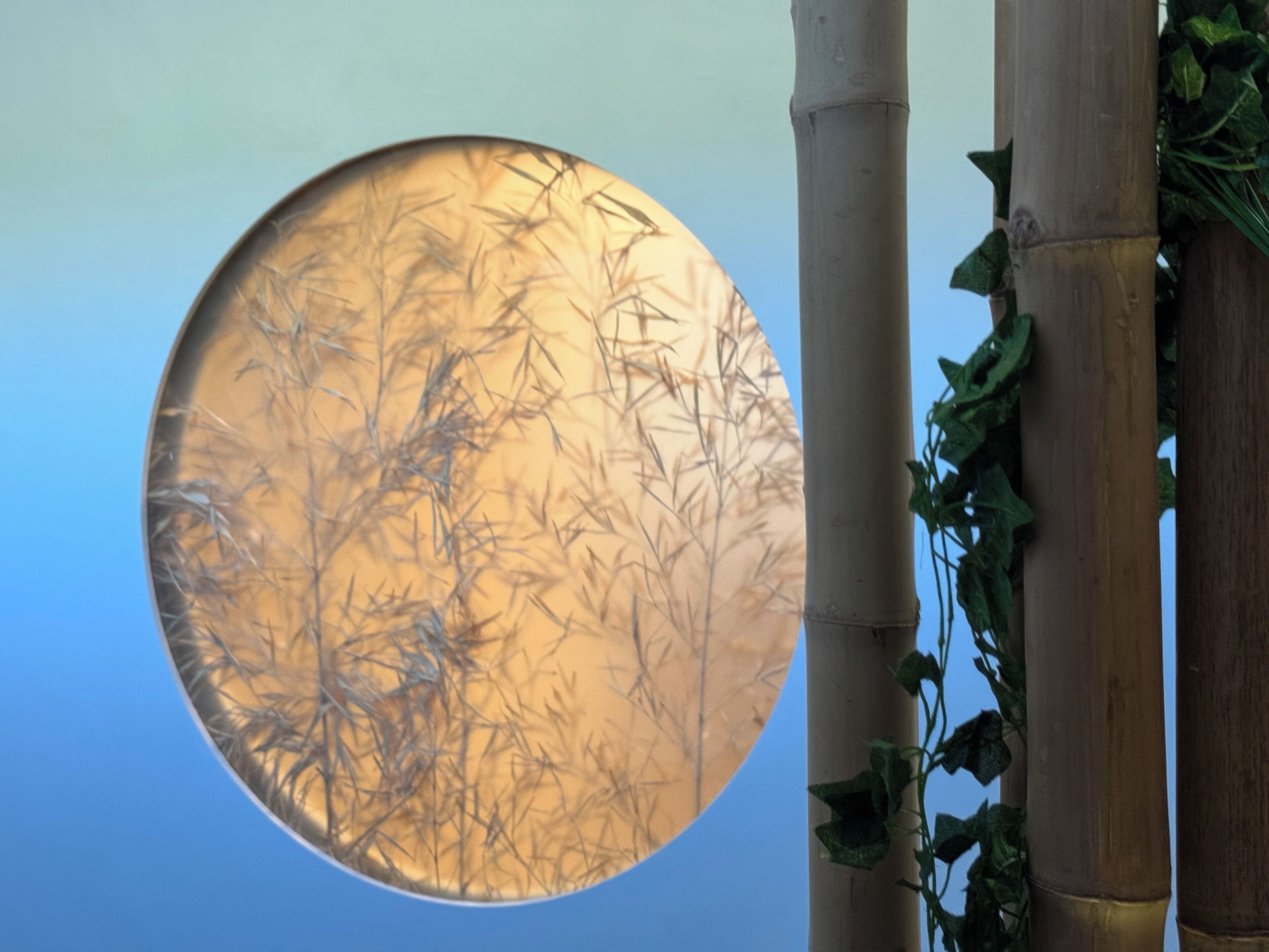 Janela circular com estrutura de bambu e vegetação lá fora.