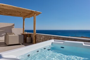 Um terraço no último andar com uma banheira de hidromassagem, uma pérgola de madeira, um sofá bege e vista para o oceano.