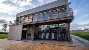 Um edifício moderno com telhado plano, janelas amplas e área externa coberta com equipamentos de ginástica.